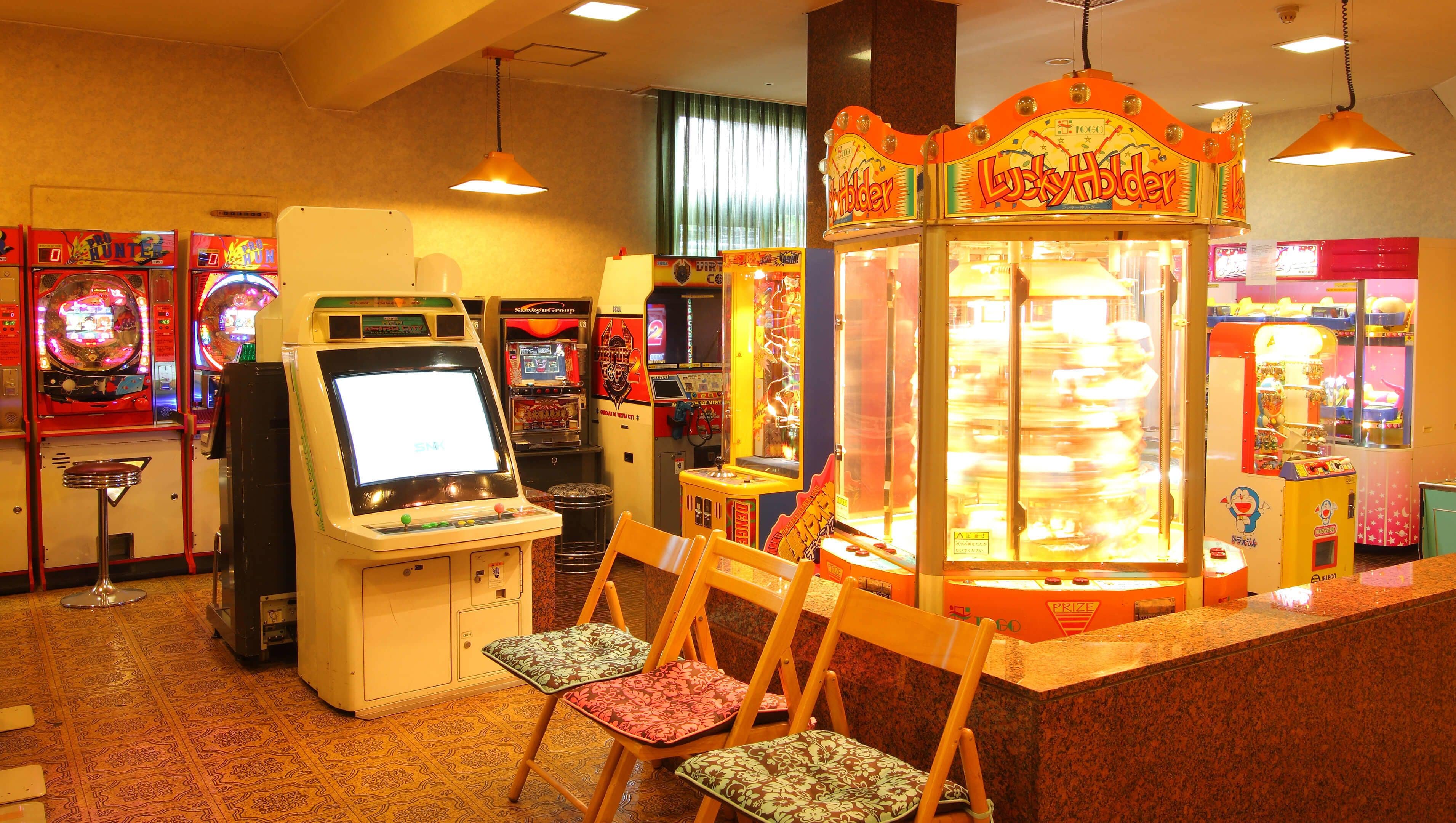 Uma sala de jogos com diversos aparelhos, uma máquina de prêmios e uma área de estar com cadeiras.