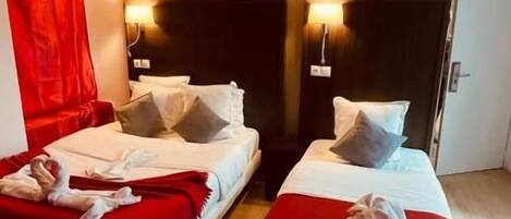 Quarto de hotel com duas camas, cada uma com colcha e almofadas vermelhas, e uma cabeceira escura.