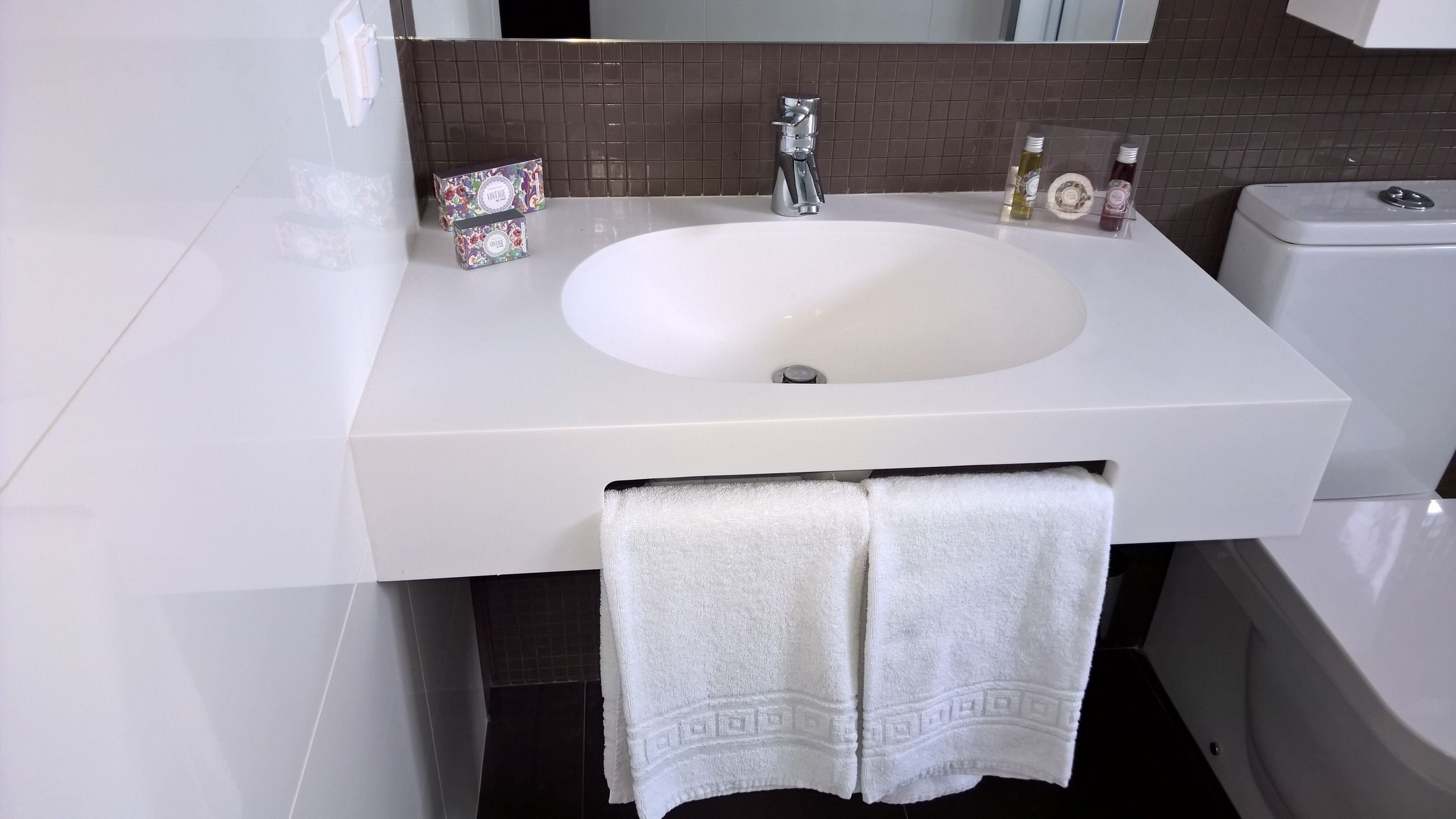 Casa de banho moderna com lavatório branco, espelho e sanita. Existem duas embalagens de sabonete e um prato decorativo no lavatório.