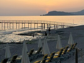 Uma praia com um cais que se estende para a água, espreguiçadeiras e guarda-sóis.
