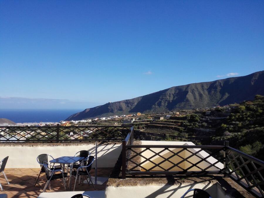 Um terraço com mesa e cadeiras, com vista para uma cidade costeira e montanhas.