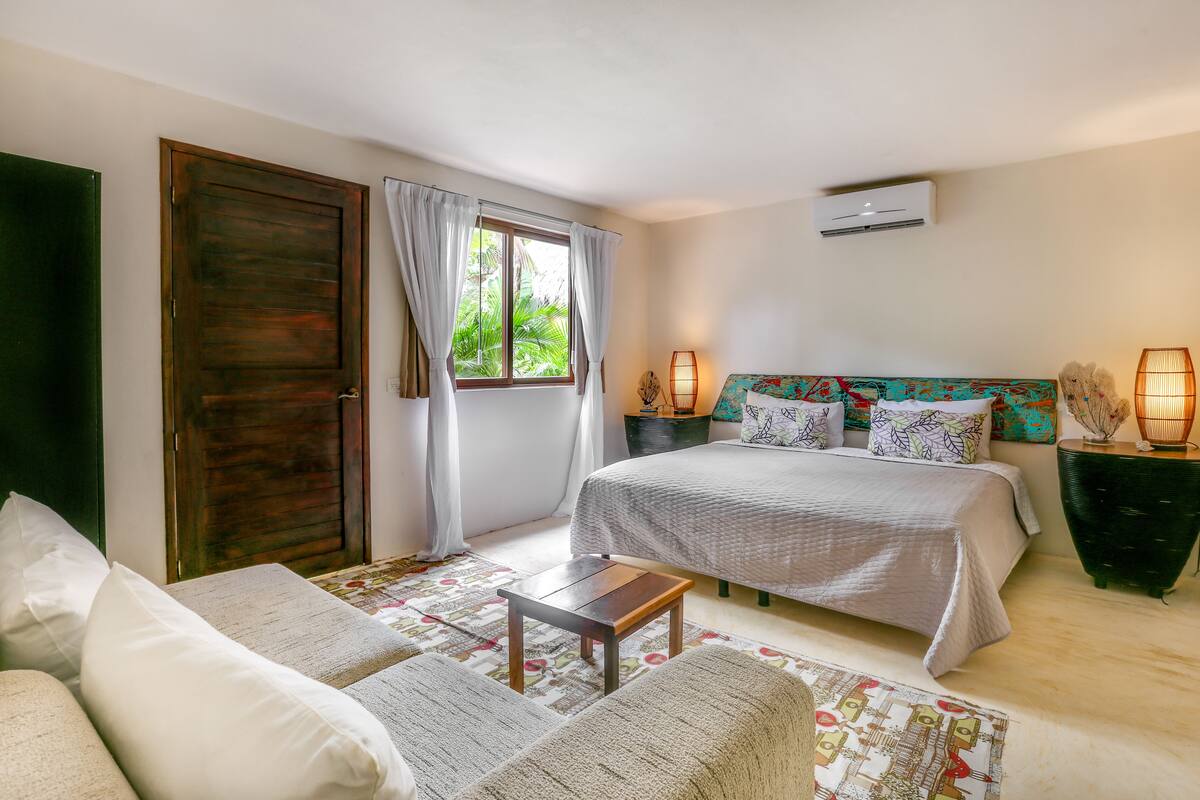 Quarto com uma cama, uma mesinha, um sofá e uma janela com cortinas.