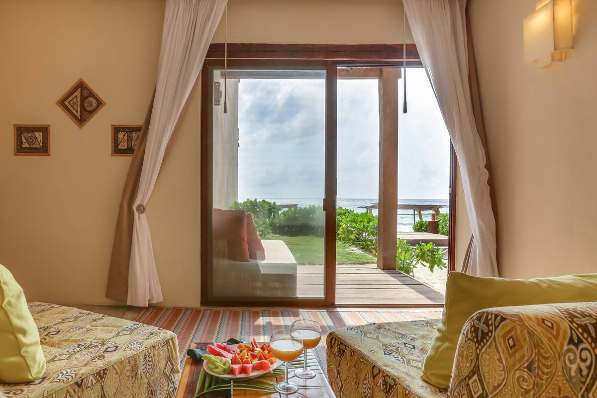 Quarto com vista para o mar, uma mesa com frutas e bebidas, e mobiliário estampado.