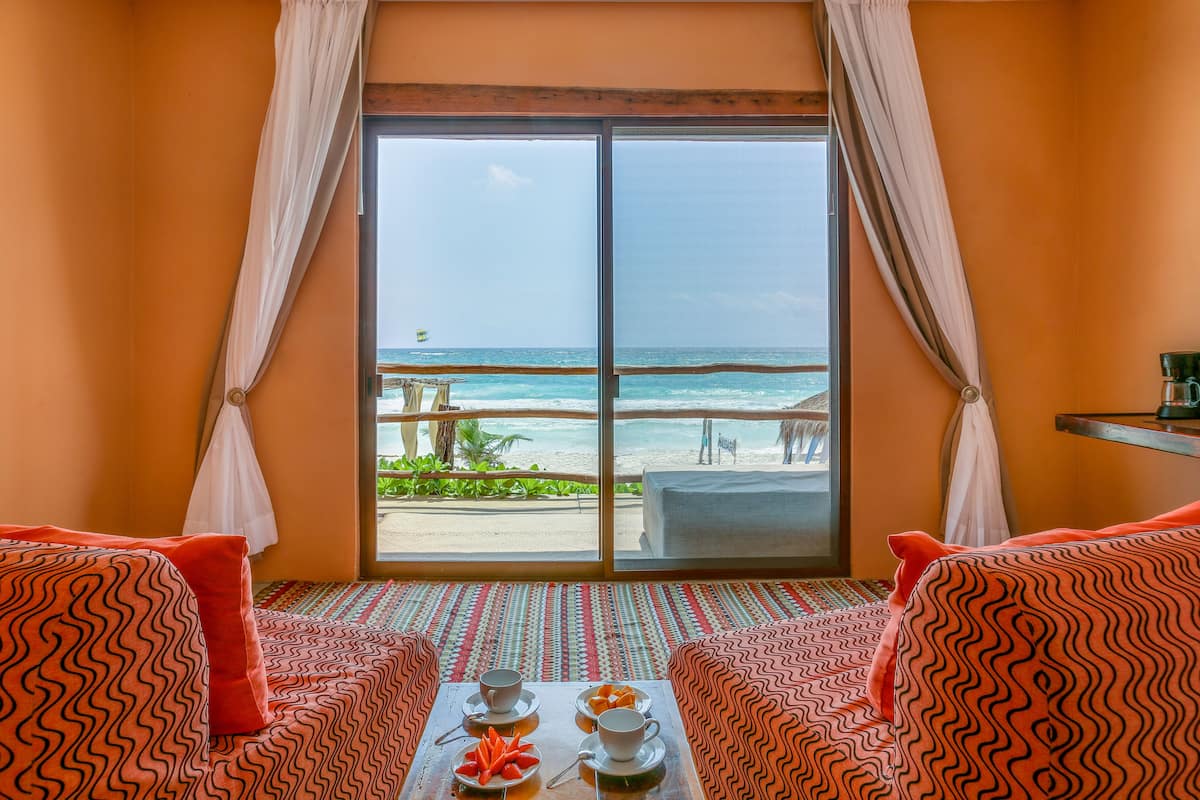 Quarto com uma grande porta de vidro deslizante que dá para a praia, duas camas com roupa de cama estampada e uma mesa com itens de café da manhã.