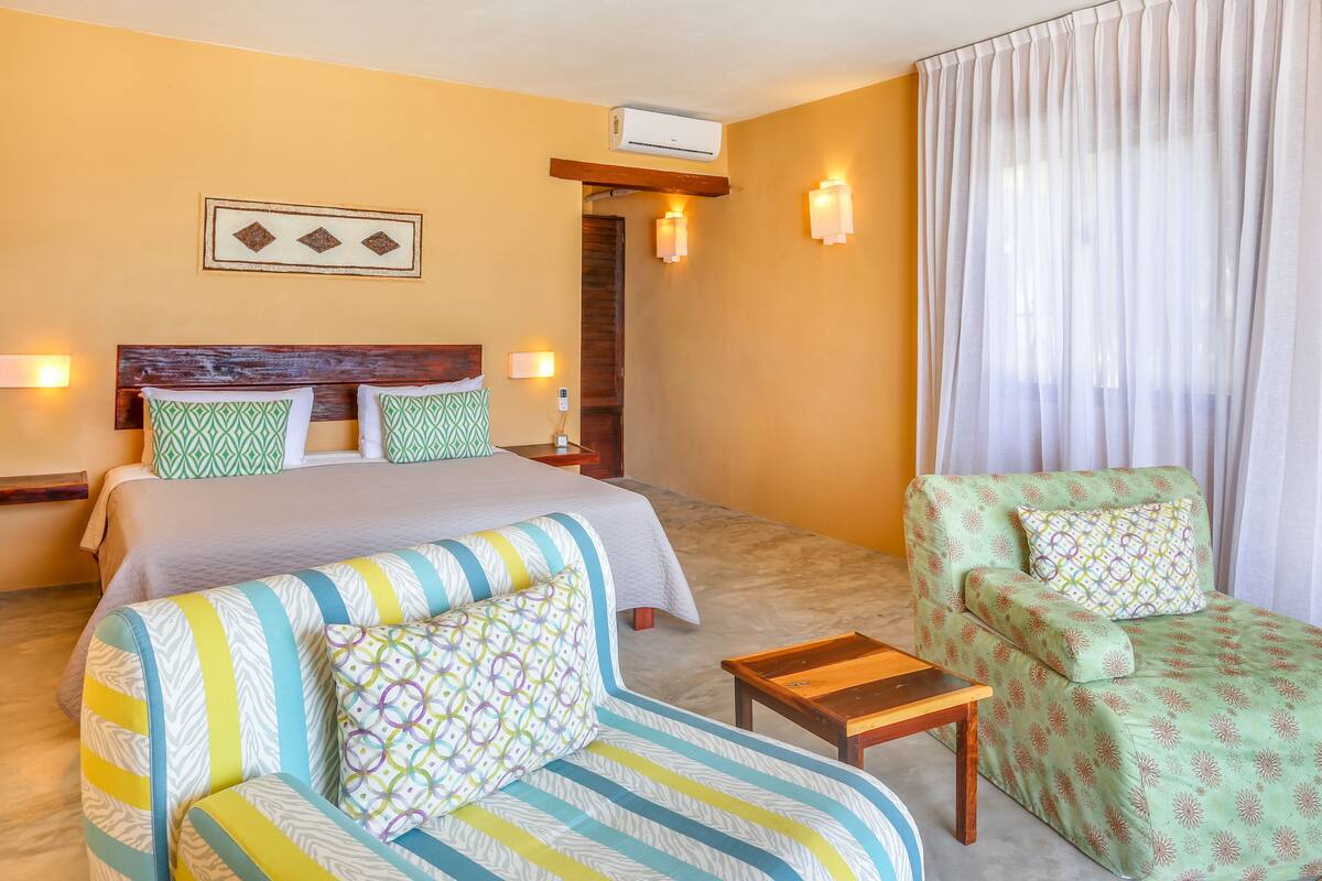 Quarto de hotel com uma cama, dois sofás, uma mesinha e uma janela com cortinas.