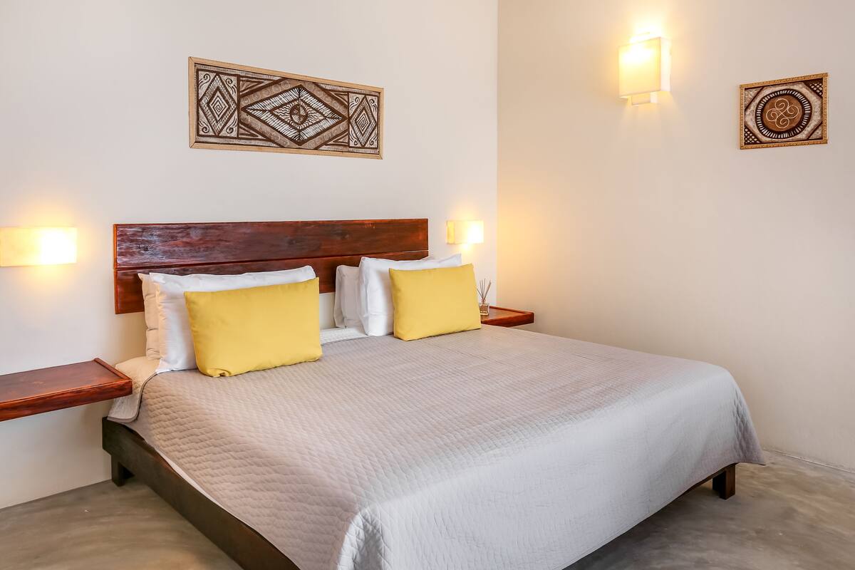 Cama bem arrumada com cabeceira de madeira, duas mesas de cabeceira com abajures e decoração na parede.