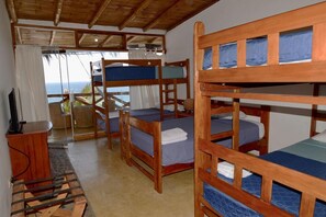Quarto com beliches, uma escrivaninha de madeira e vista para o oceano.