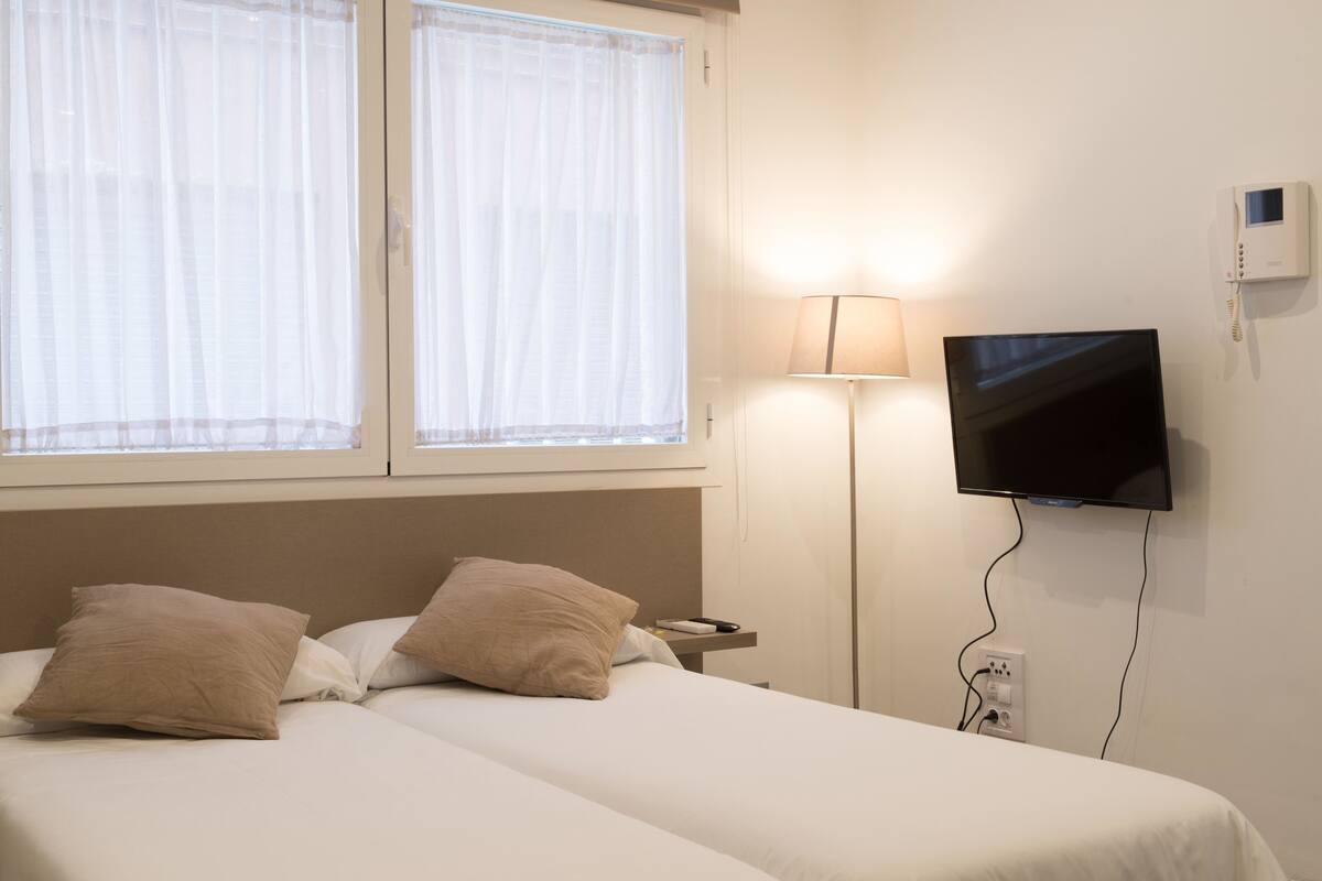 Quarto de hotel com duas camas, televisão, mesa de cabeceira e abajur.