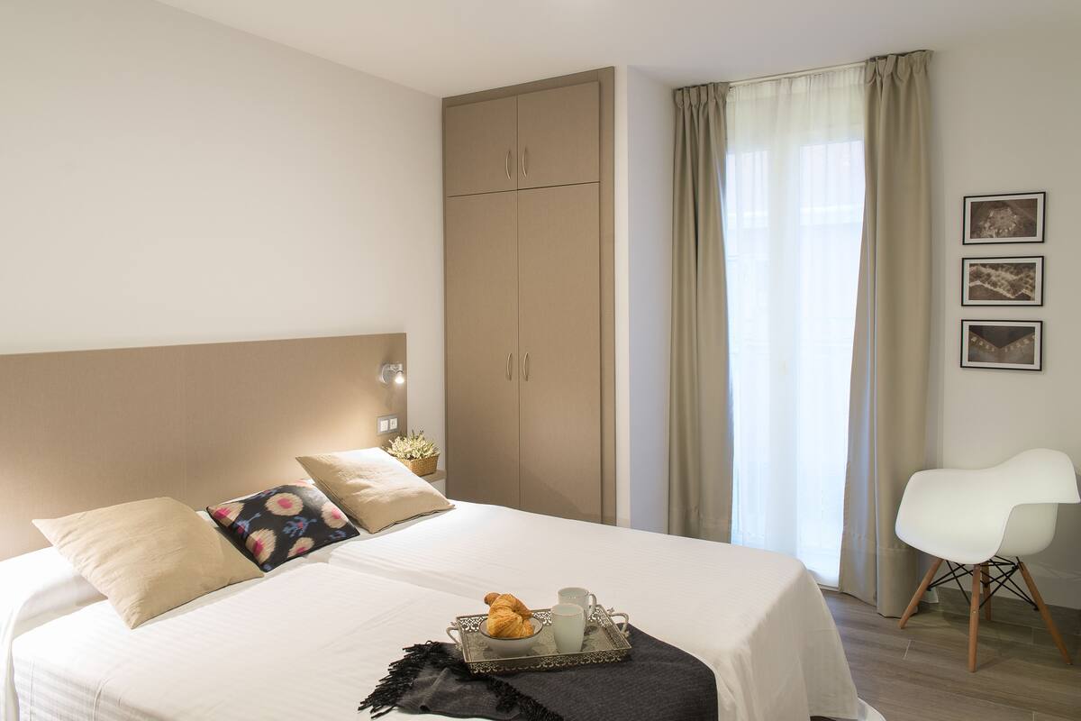 Quarto com cama, guarda-roupa, uma cadeira e um tabuleiro com um croissant e uma chávena.