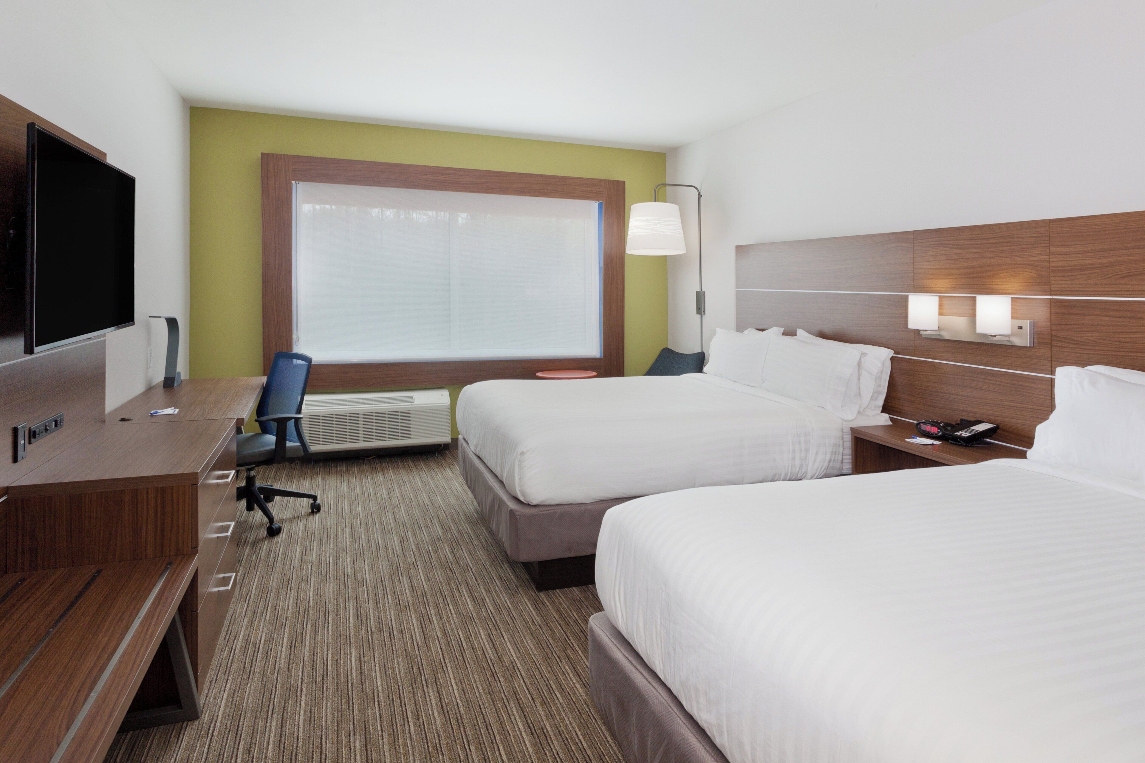 Quarto de hotel com duas camas, uma escrivaninha, televisão, uma cadeira e janela com persianas.