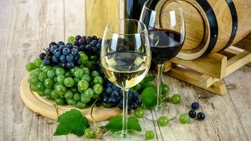 Um barril de madeira, duas taças de vinho e uma tábua com uvas verdes e escuras.