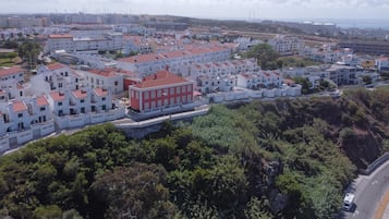 Área residencial com edifícios brancos e telhados vermelhos, rodeada por vegetação e uma estrada.