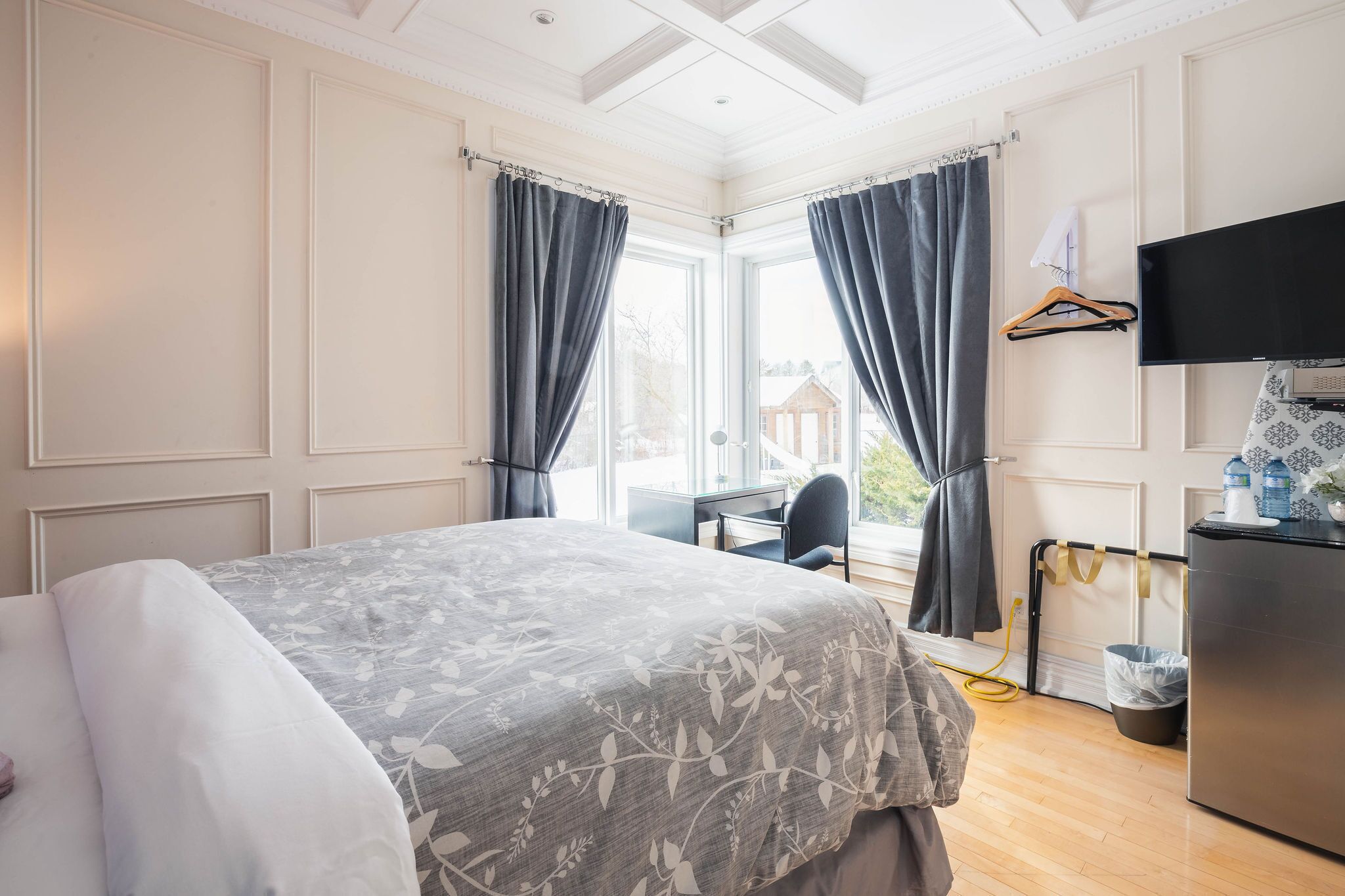 Quarto de hotel com cama, escrivaninha, cadeira, televisão e janela com cortinas.