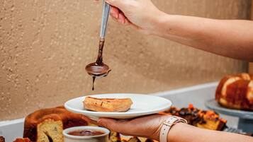 Uma mão segurando um prato com uma fatia de bolo e uma colher com calda de chocolate.