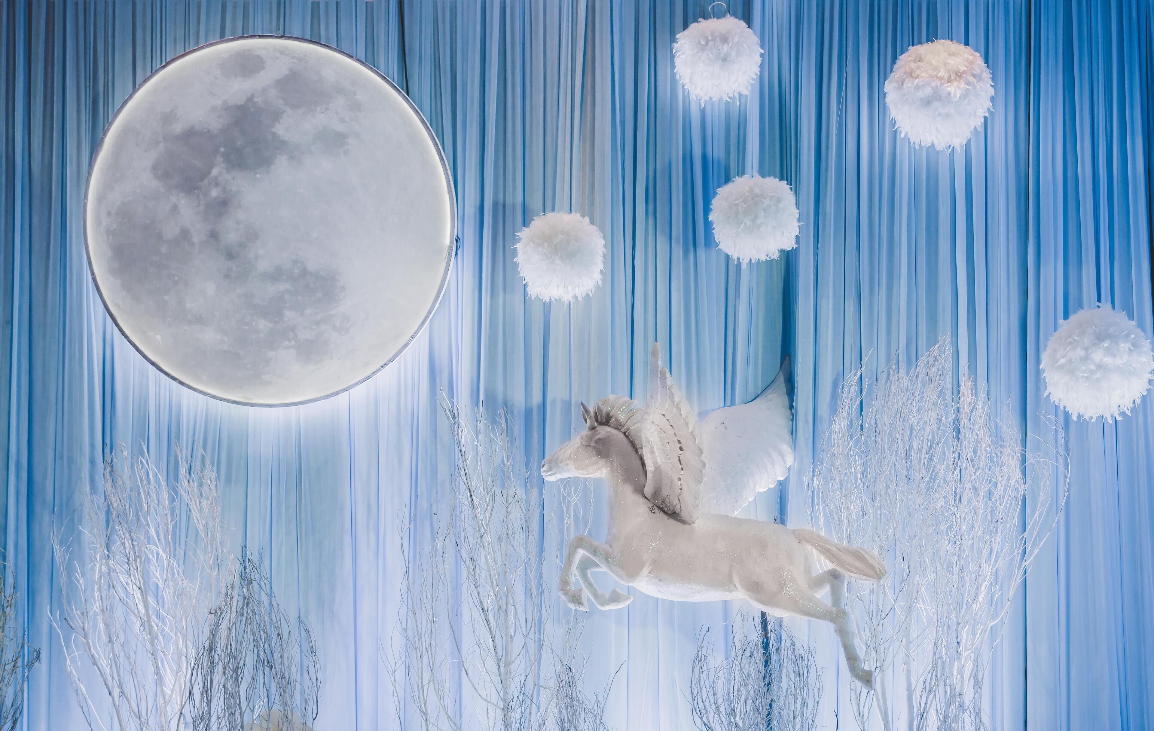 Quarto com uma grande lua, uma escultura de cavalo branco e um fundo listrado em azul.
