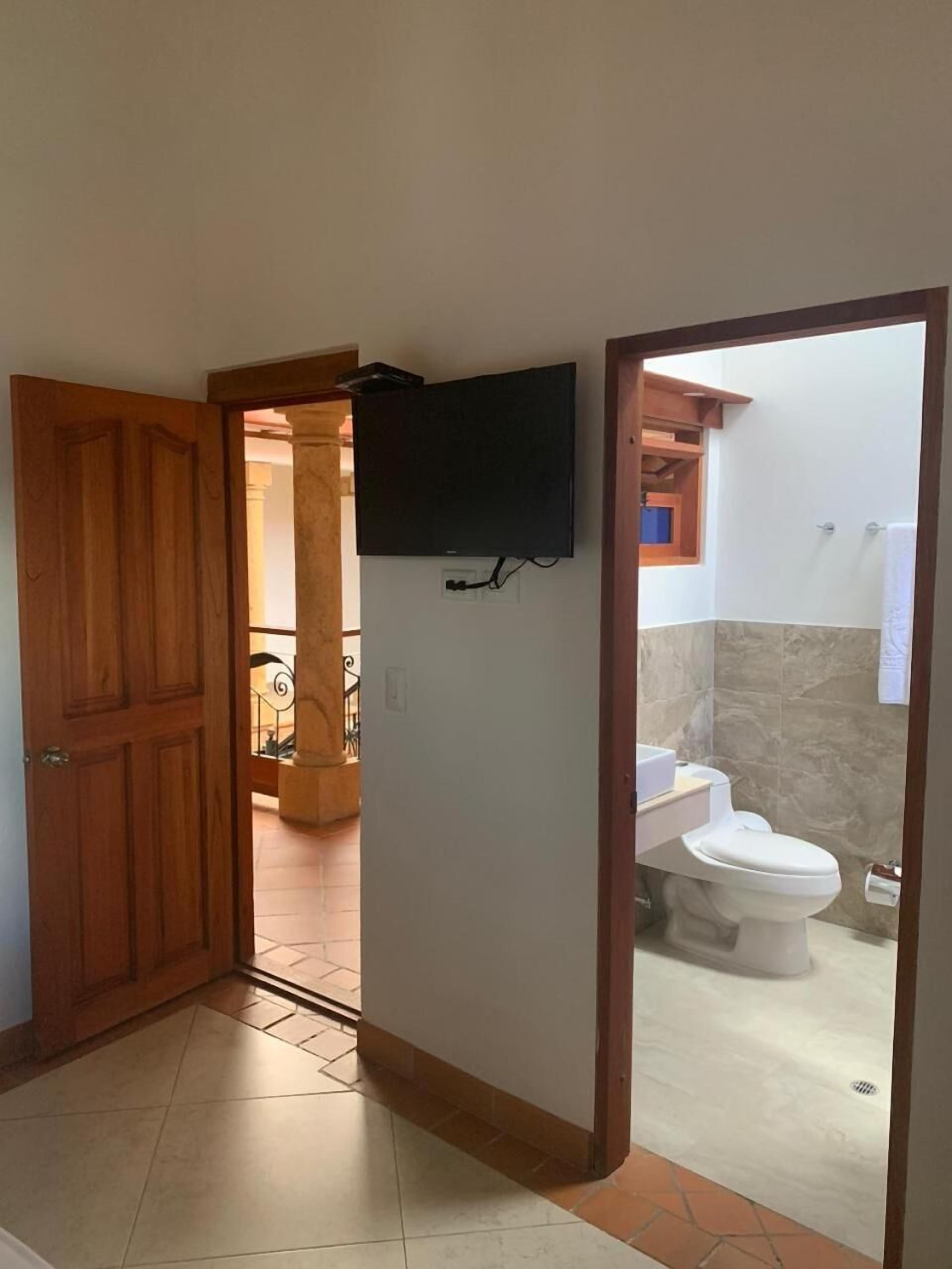 Corredor que dá acesso a um banheiro com vaso sanitário e área de chuveiro.