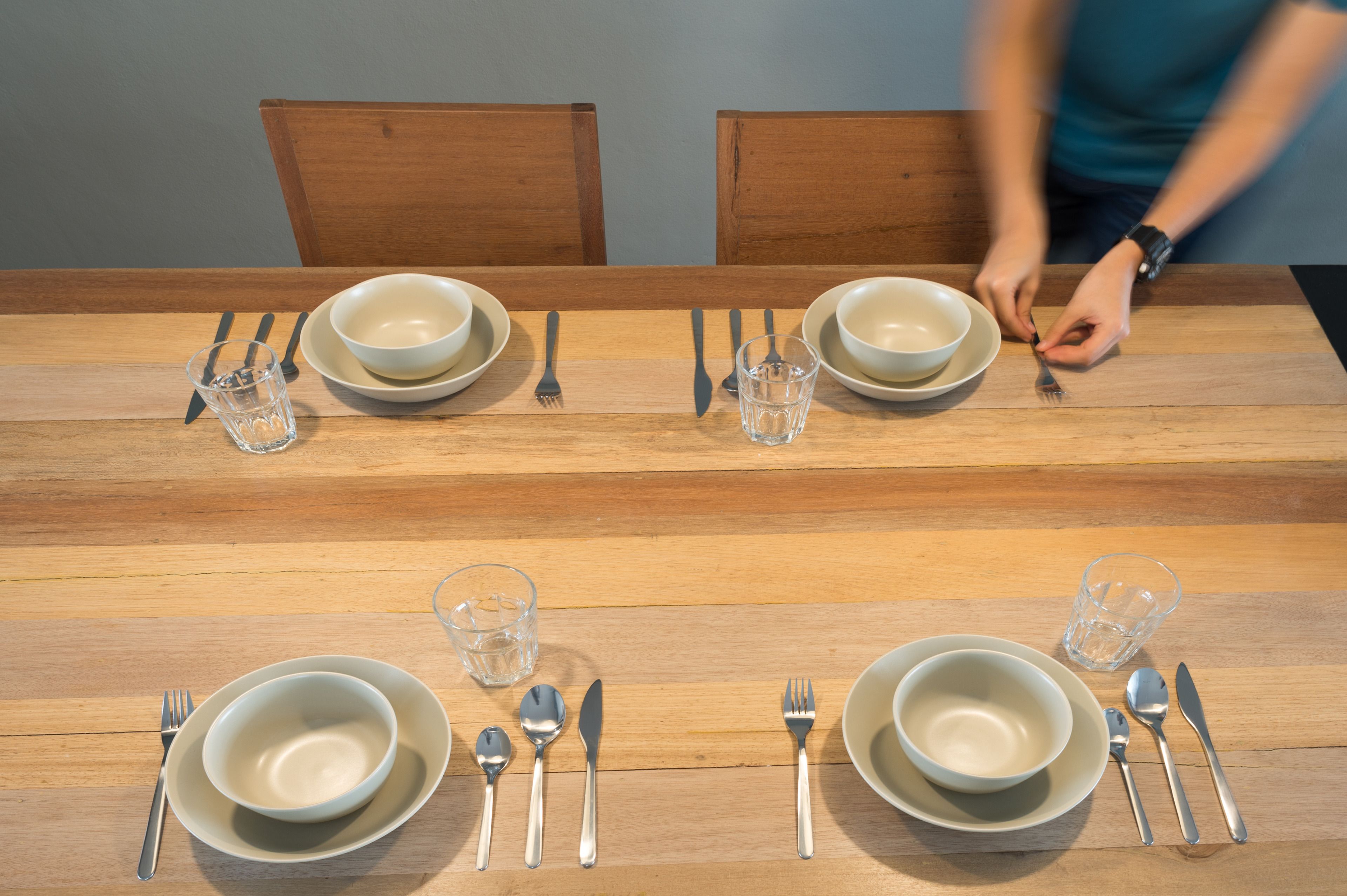 Mesa de jantar de madeira posta com pratos, tigelas, talheres e copos.