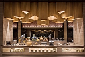 Uma área de buffet bem iluminada com diversas opções de comida e bebida, incluindo uma máquina de café e uma seleção de pratos e tigelas.
