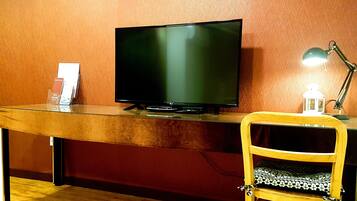 Uma mesa de madeira com uma TV de tela plana, uma luminária e uma cadeira com almofada estampada.
