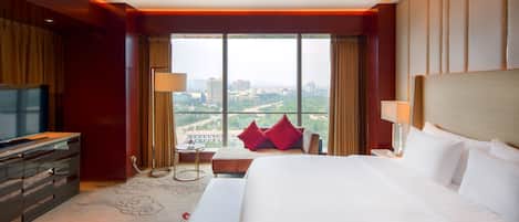 Quarto de hotel com uma cama grande, televisão, escrivaninha e vista para a cidade.