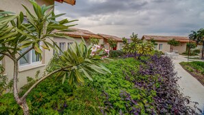 Uma fileira de villas com um jardim em primeiro plano, um caminho e vista do céu.