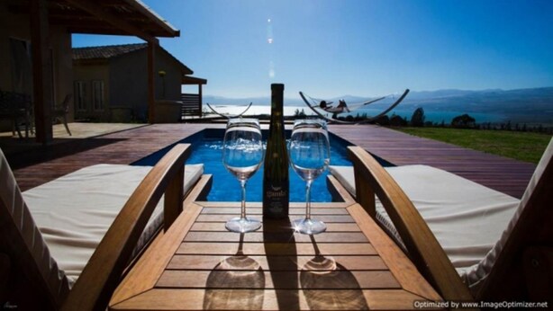 Um deck de madeira com duas cadeiras de descanso e uma piscina, com vista para uma paisagem montanhosa.