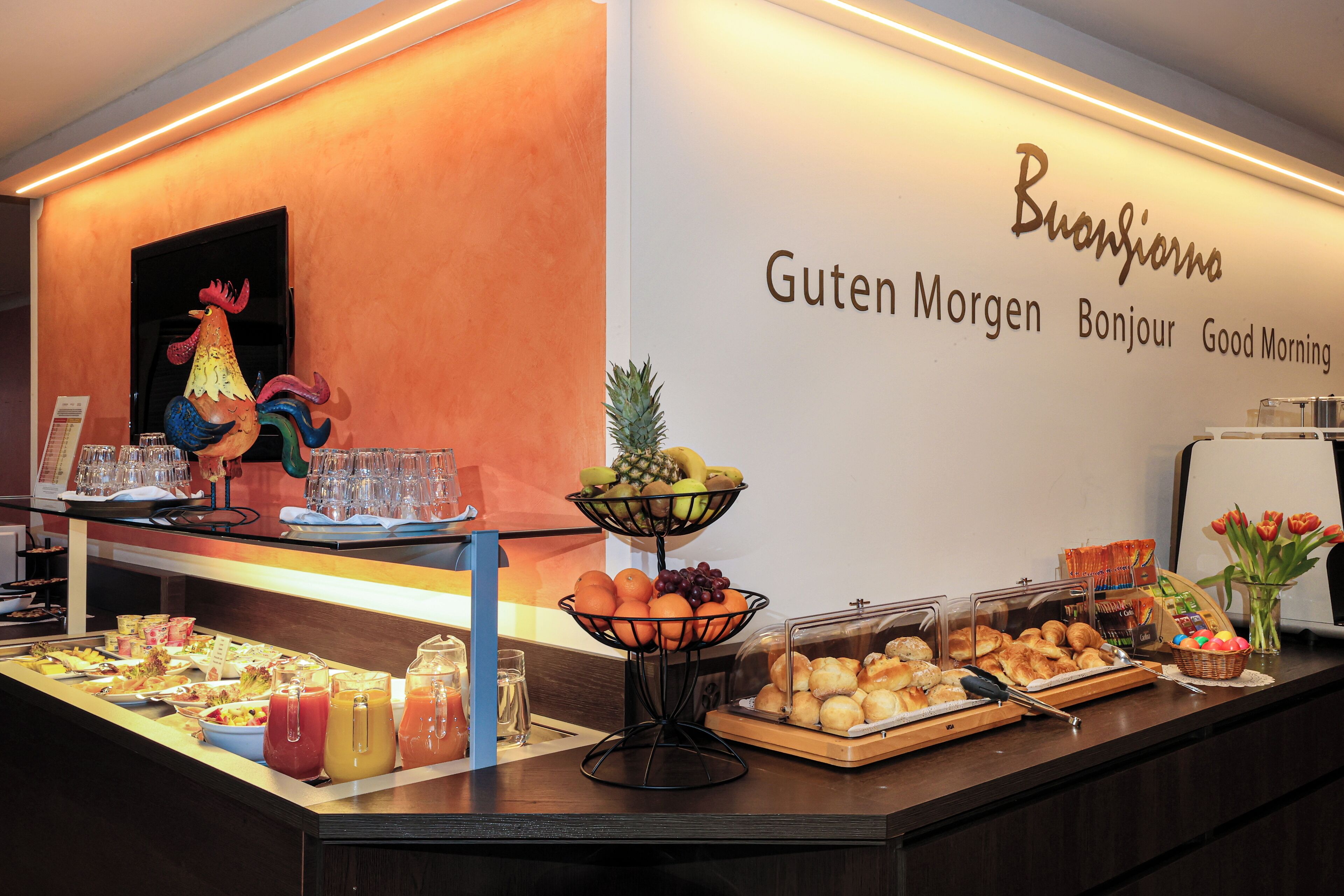 Um buffet de café da manhã com diversas opções de comida, uma cesta de frutas e um galo decorativo.