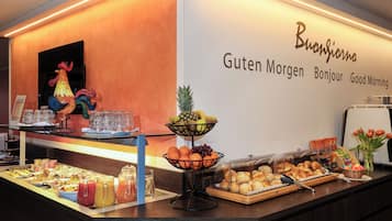 Um buffet de café da manhã com diversas opções de comida, uma cesta de frutas e um galo decorativo.