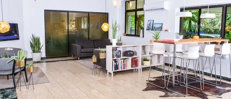 Uma sala de estar moderna com sofá, mesa de centro, estante e um espaço de jantar com banquetas.