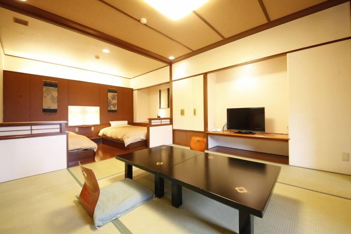 Quarto de hotel com tatames, cama, escrivaninha, televisão e parede no estilo tradicional japonês.