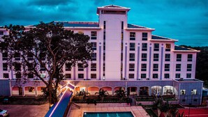 Um hotel com piscina, vários andares e uma grande árvore em frente.