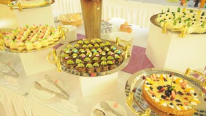 Buffet com diversos doces e um bolo em vitrine de vidro.