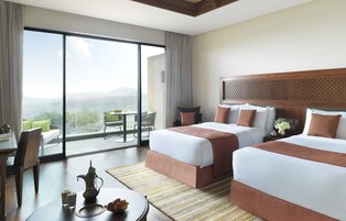 Quarto de hotel com duas camas, área de refeições e varanda com vista.