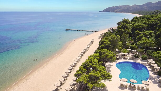 Um resort à beira-mar com piscina, guarda-sóis e espreguiçadeiras.