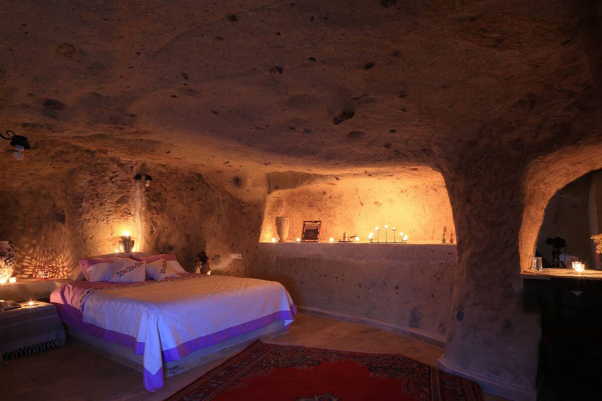 Um quarto com formato de caverna, com uma cama, abajures e um tapete vermelho.