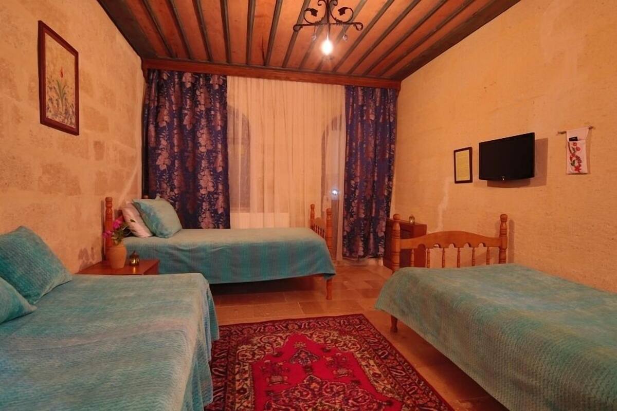 Quarto com duas camas, teto de madeira, televisão e janela com cortinas.
