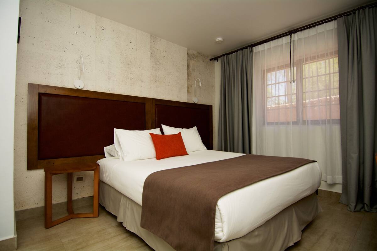 Cama bem arrumada com manta marrom, mesa de cabeceira de madeira e cabeceira.