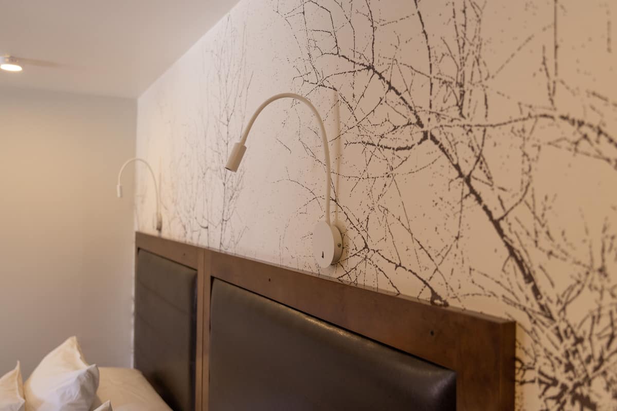 Quarto com cabeceira, luminária na parede e parede com design de galho de árvore.