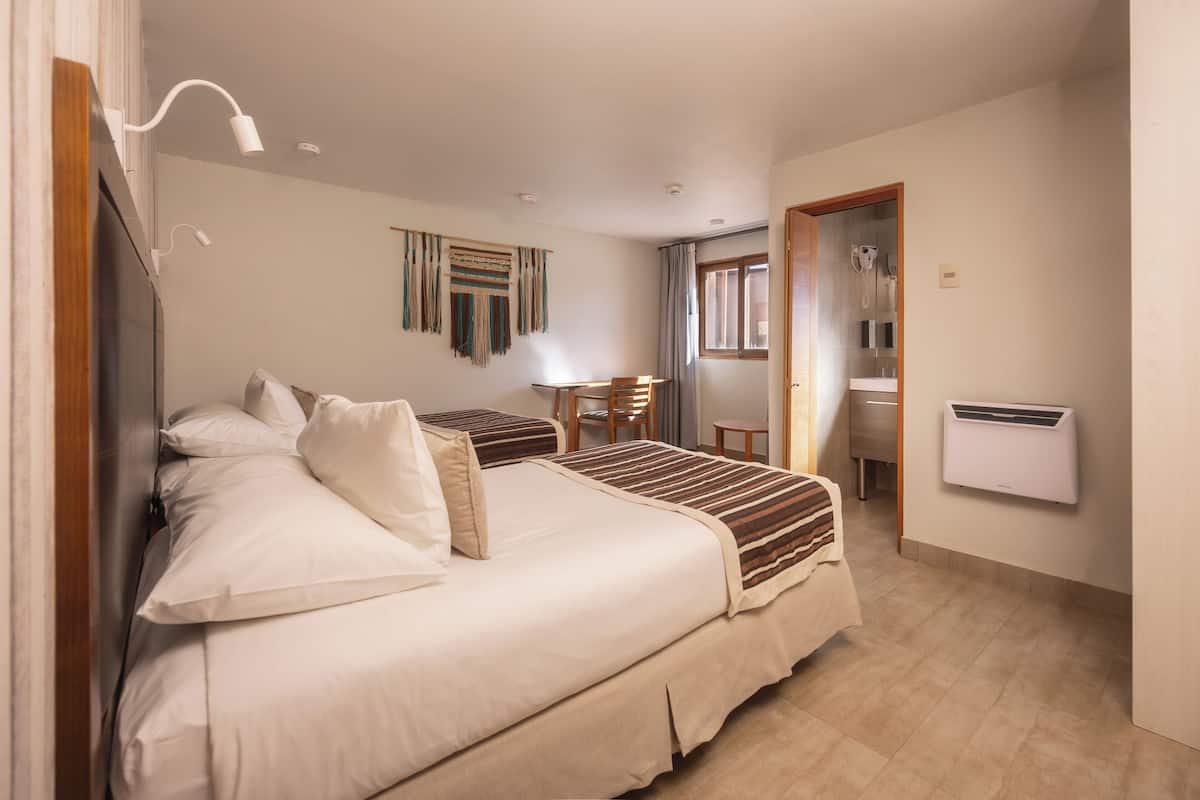 Quarto de hotel com uma cama, escrivaninha, cadeira, telefone fixado na parede e ar condicionado.