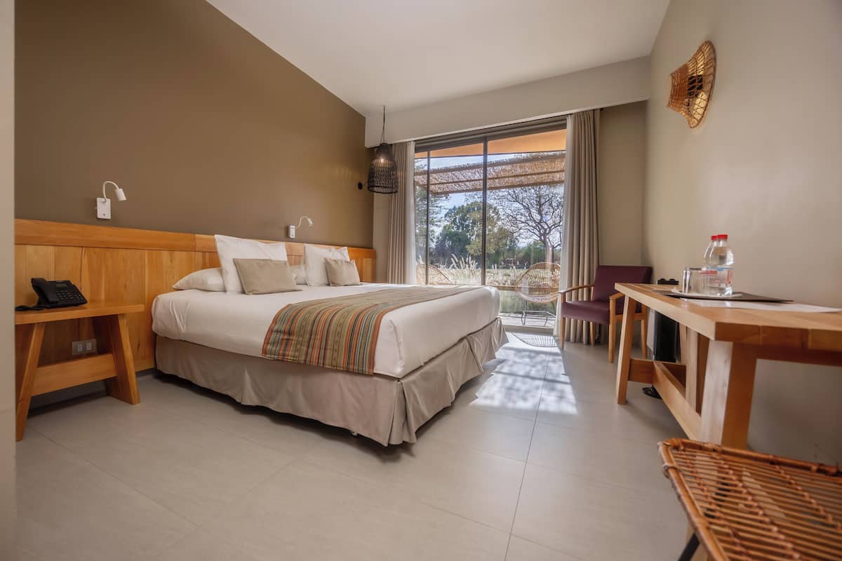 Quarto de hotel com cama, mesa de cabeceira, luminária e vista para o exterior.