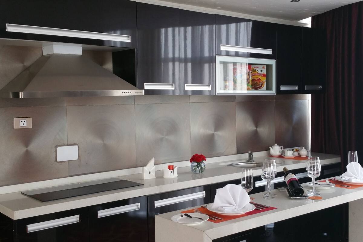 Cozinha moderna com eletrodomésticos de aço inoxidável, forno embutido e micro-ondas. Há uma área de refeições com mesa posta para dois, incluindo copos de vinho, pratos e talheres.