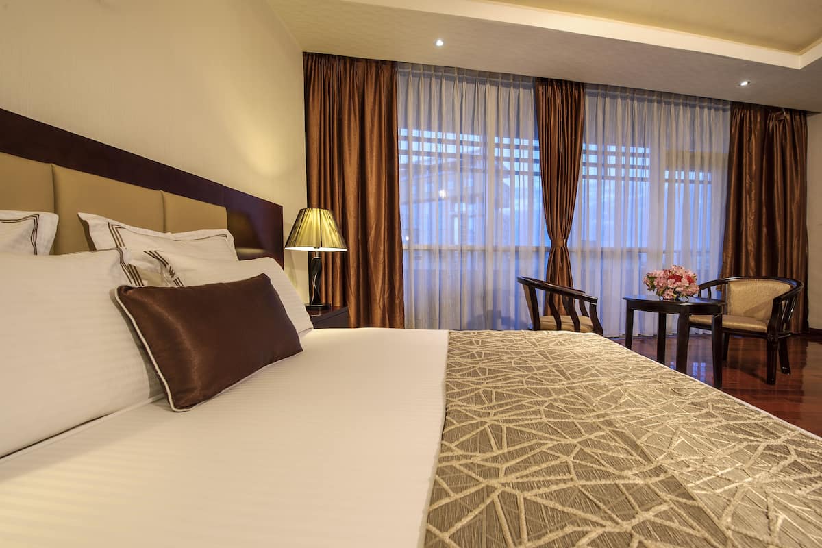 Quarto de hotel com uma cama grande, uma mesa de cabeceira com abajur, uma pequena mesa com um vaso de flores e uma cadeira.