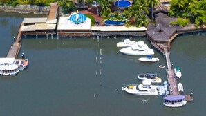 Vista aérea de um resort à beira-mar com marina, várias piscinas e vegetação exuberante.