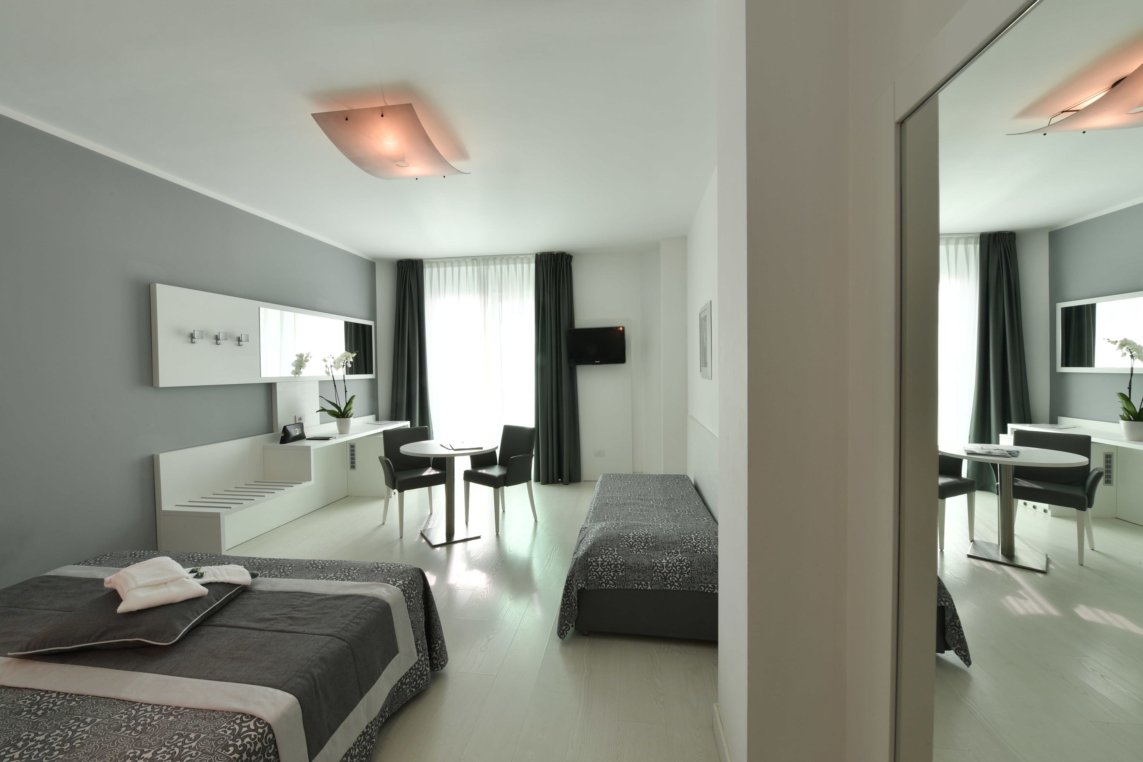 Quarto de hotel moderno com uma cama grande, uma escrivaninha, uma cadeira e uma mesinha.