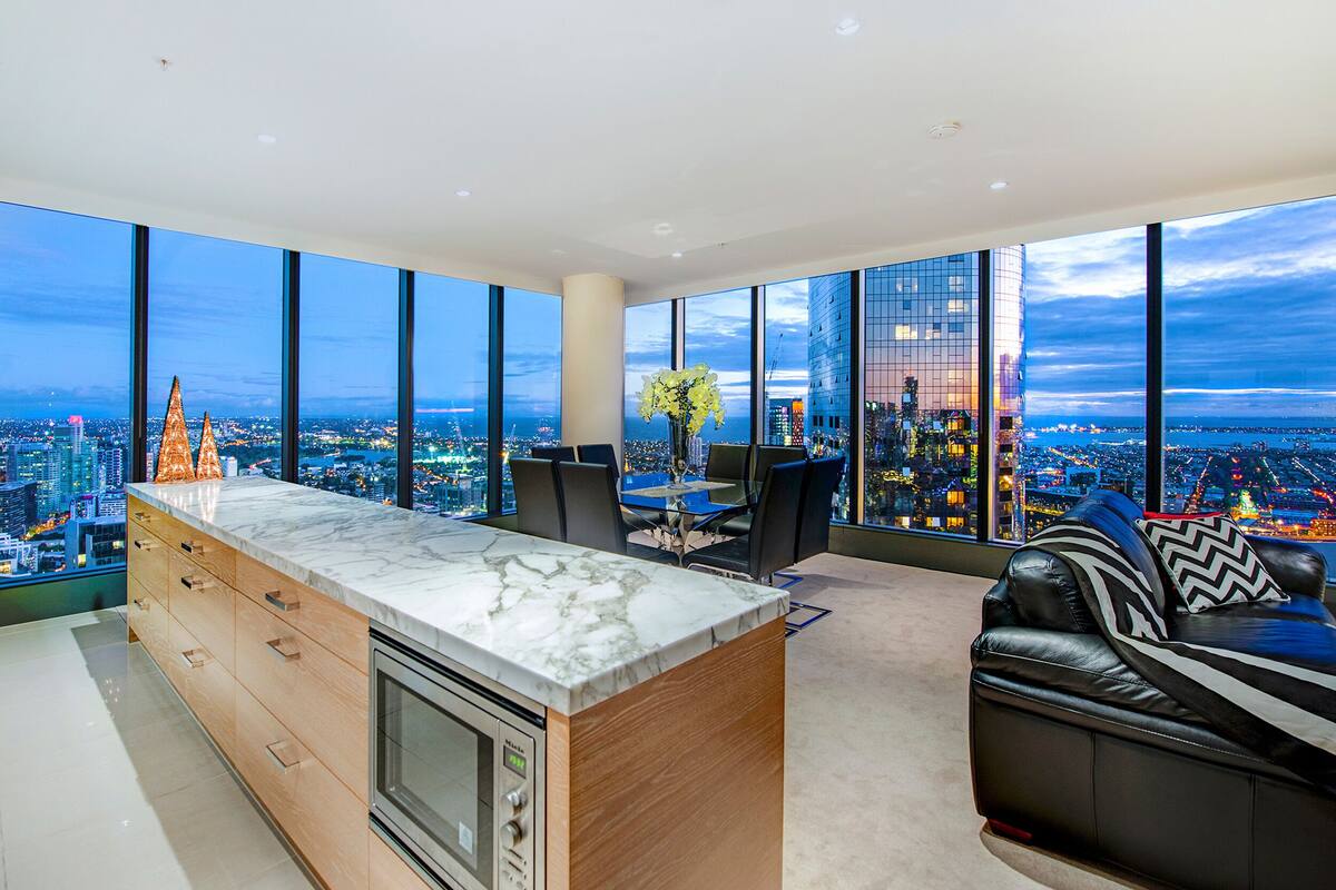 Cozinha moderna com bancada de mármore, forno embutido e uma grande janela com vista para a paisagem urbana.