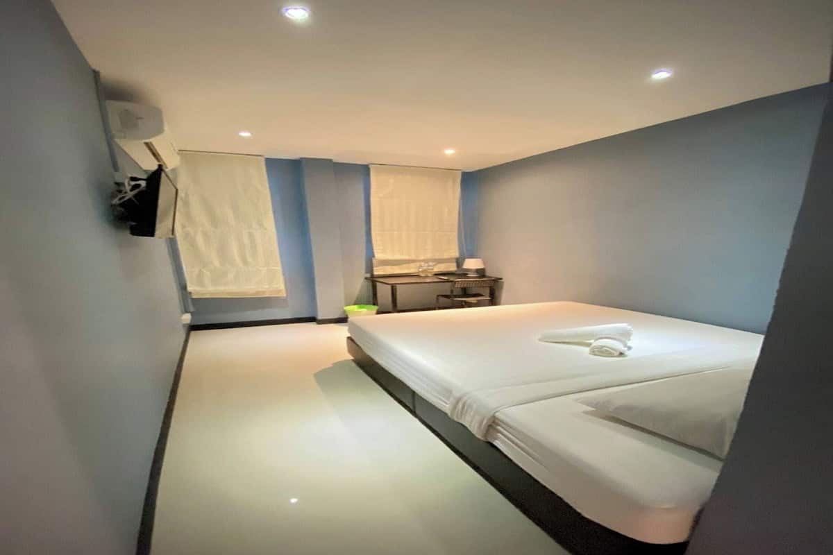 Quarto de hotel com cama, escrivaninha, cadeira, espelho e janela com cortinas.