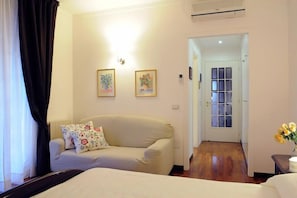 Quarto de hotel com sofá, cama e corredor que leva a uma porta.