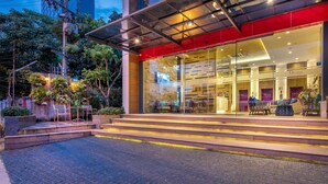 Uma entrada de hotel moderna com fachada de vidro, área de estar externa e toldo vermelho.