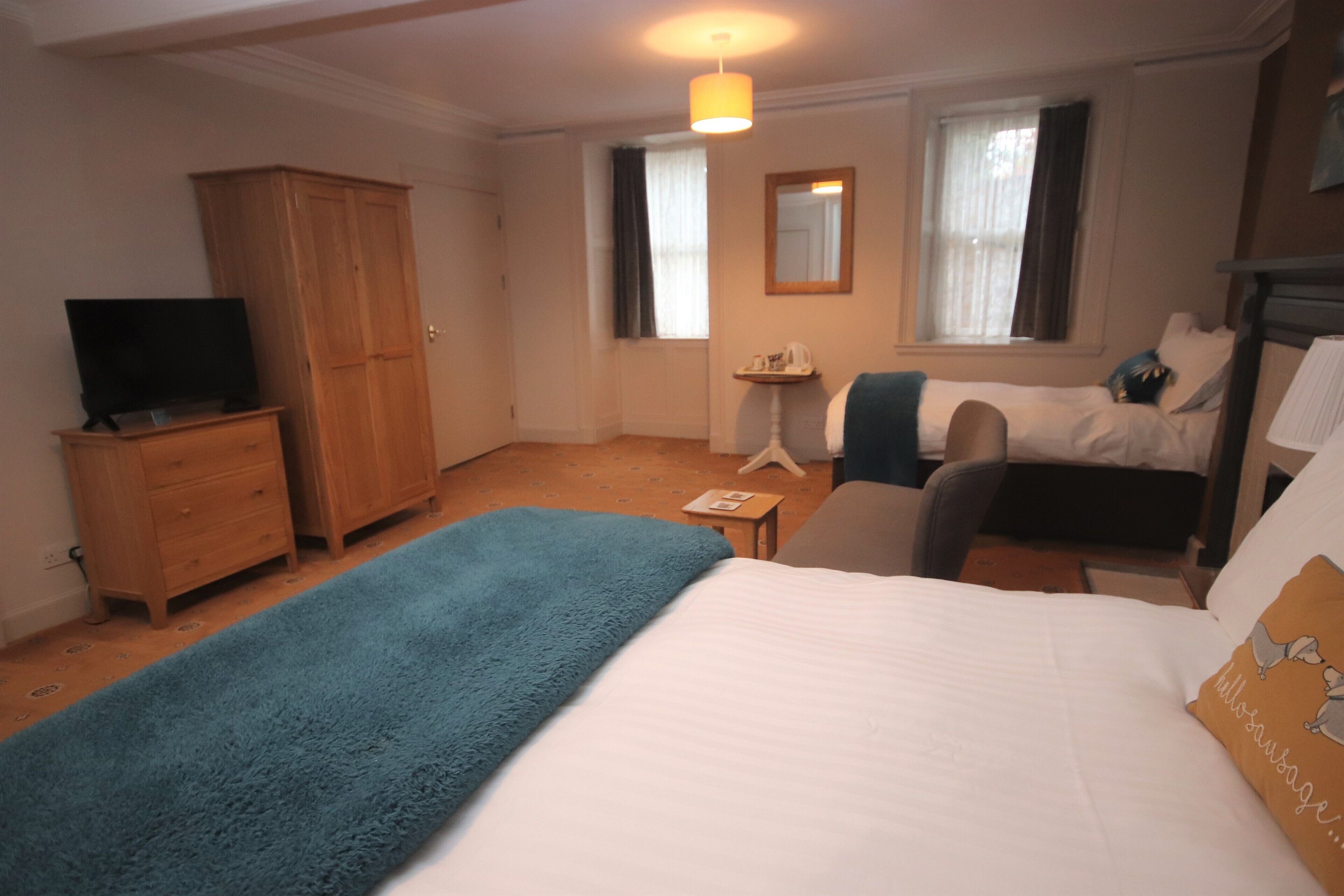 Quarto de hotel com cama, televisão, guarda-roupa, uma pequena mesa e janela com cortinas.
