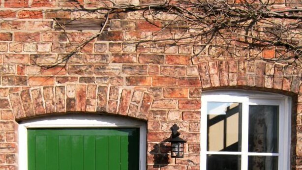Um edifício de tijolos com porta verde e janela emoldurada por branco.